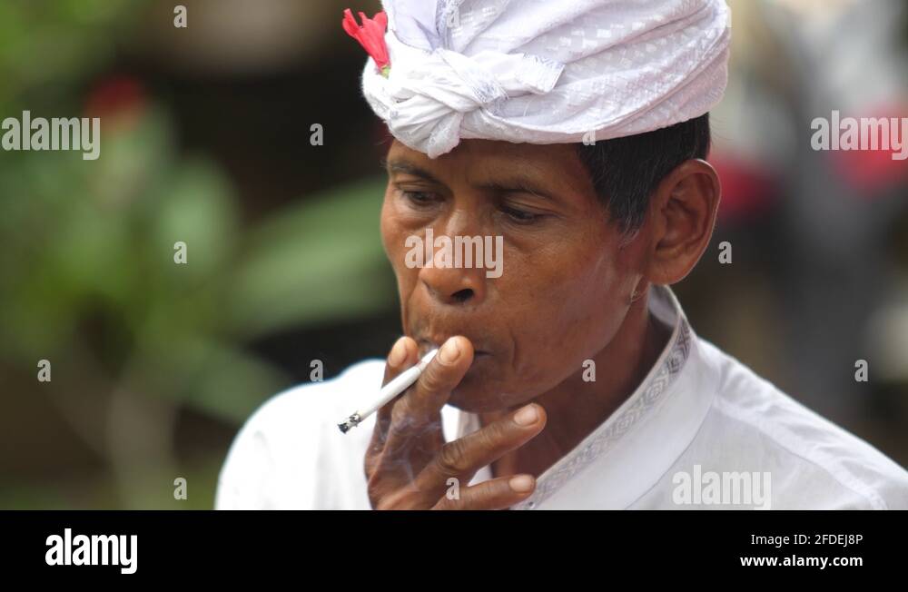 Close up view of Balinese man smoking cigarette. Man dressed in white ...
