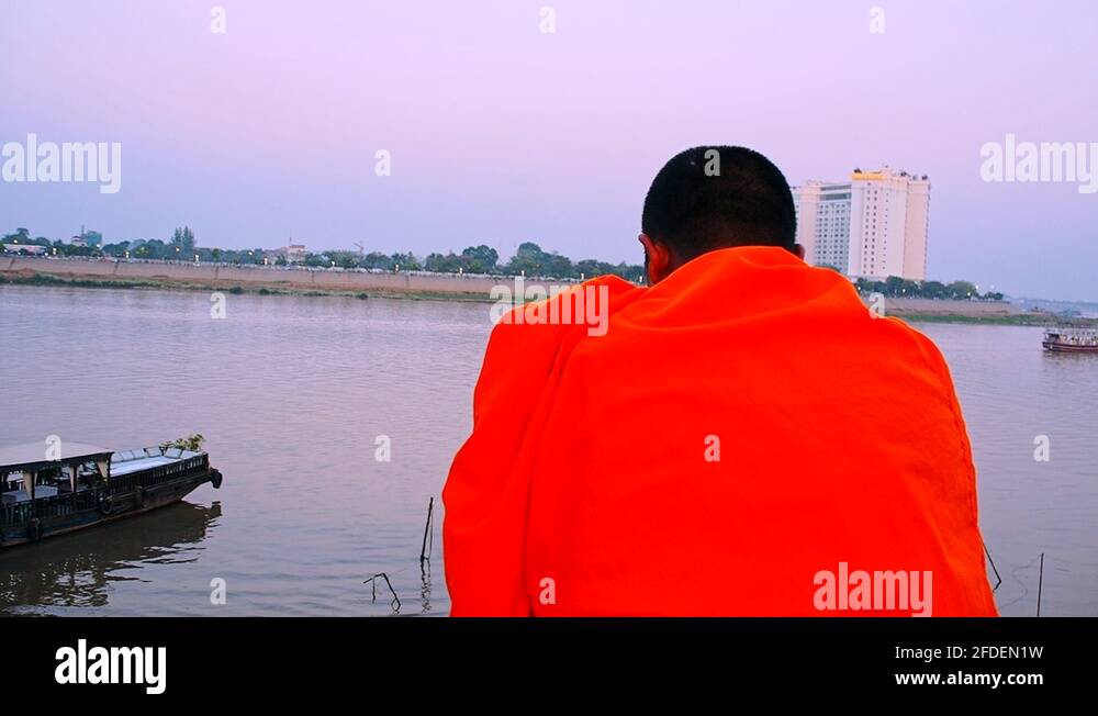 A Buddhist monk wearing a traditional orange cloak standing by the ...