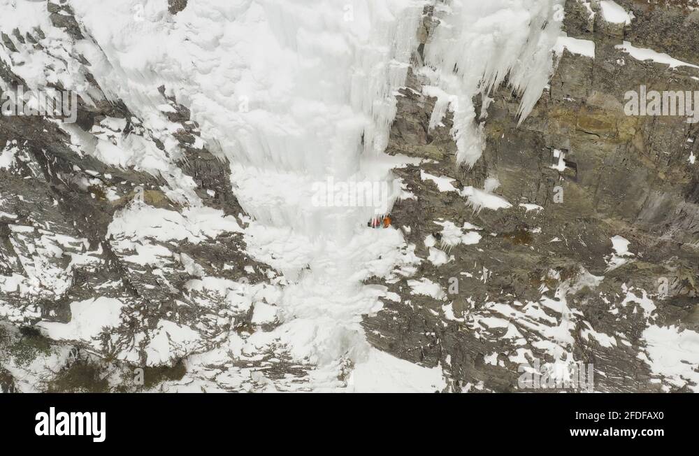Sheer cliff frozen cascade climbers under overhang on ledge Aerial 4K ...