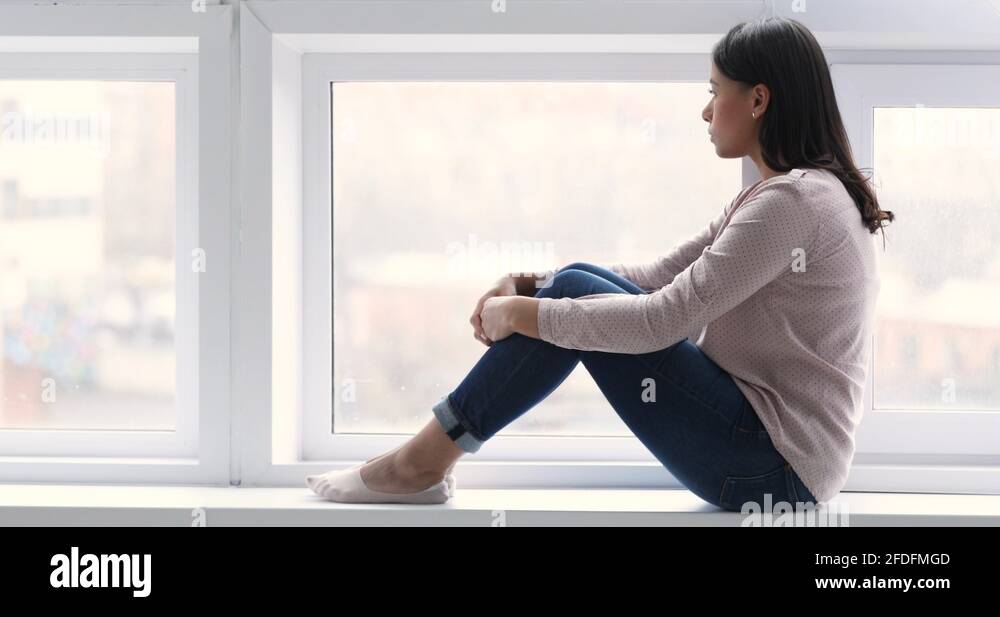 Thoughtful african american woman sit on sill looking through window ...