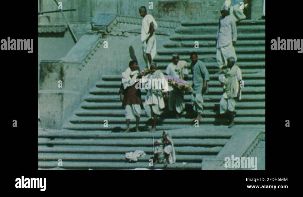 1960s: Men carry wrapped corpse down stone steps. Men arrange logs on ...