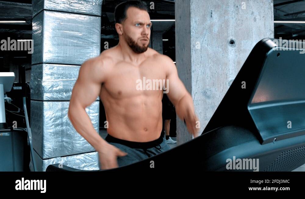 A bearded attractive young man bodybuilder running on the running track ...