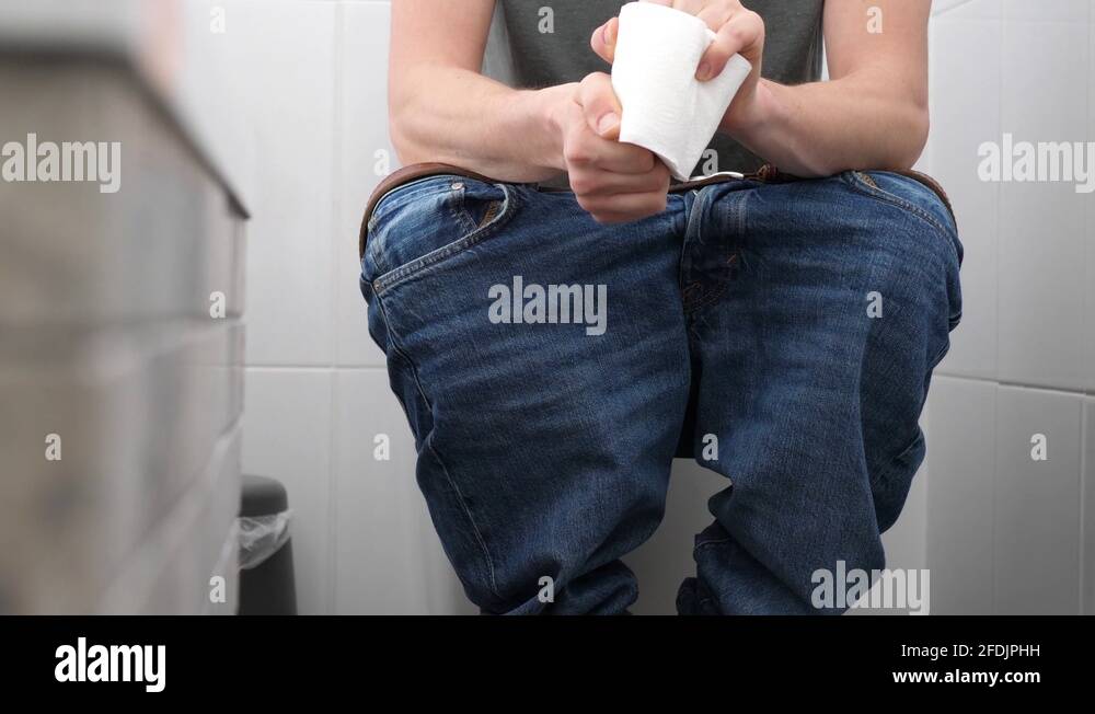 A man with trousers down sitting on the toilet has problems with Stock ...