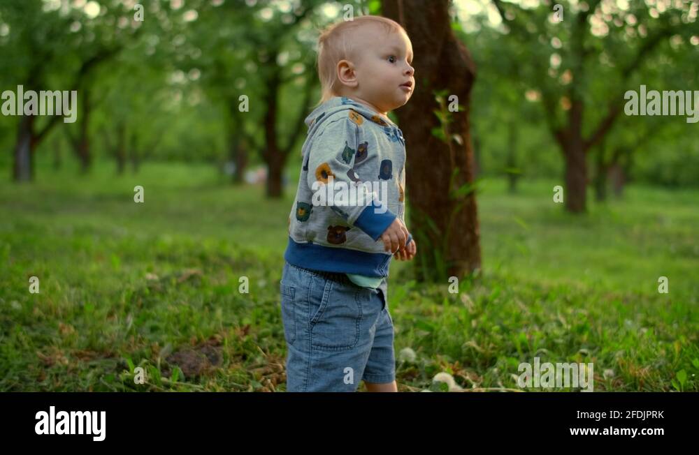 Cute kid boy falling on ground outdoors. Little baby standing in green ...