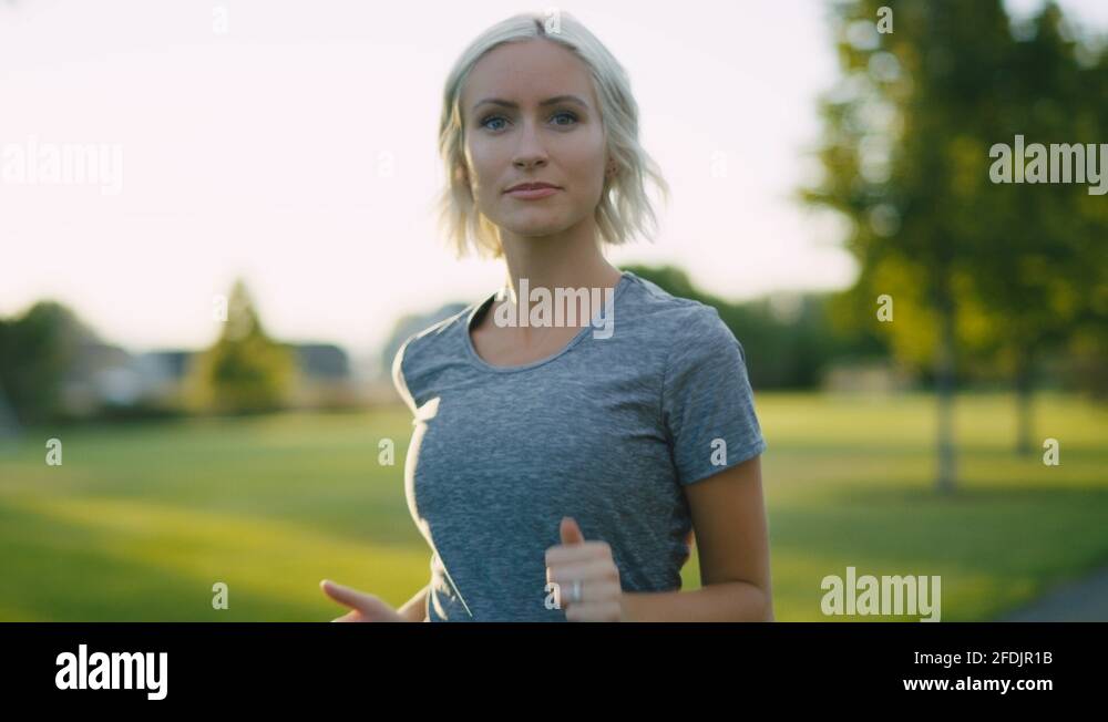 Beautiful blonde jogger runs along park path with big sun flares in ...