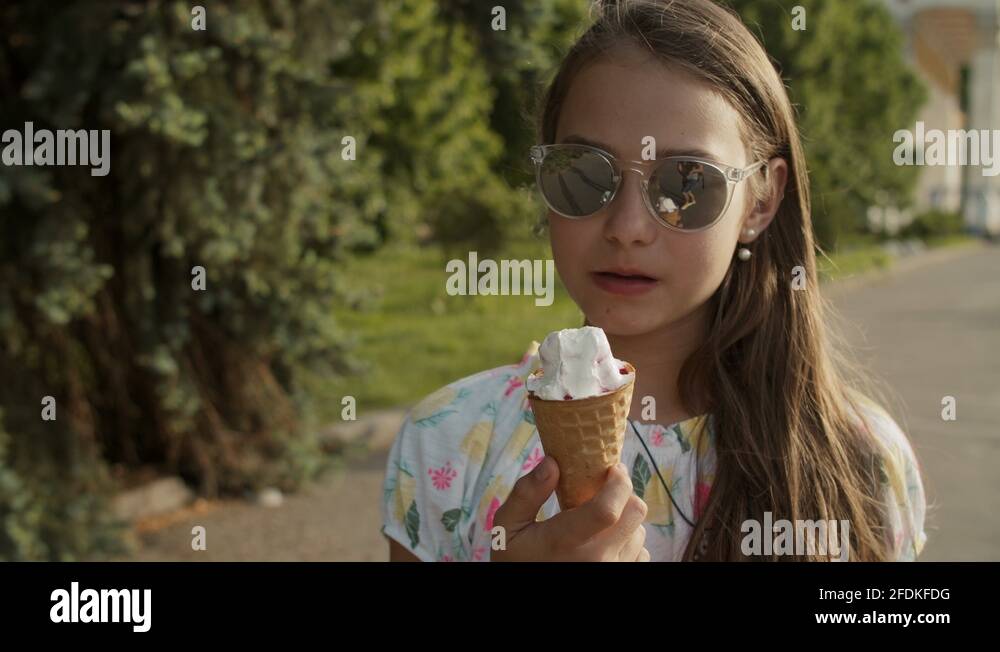 Relaxed teenage girl walking in amusement park. Cute girl eating ice ...