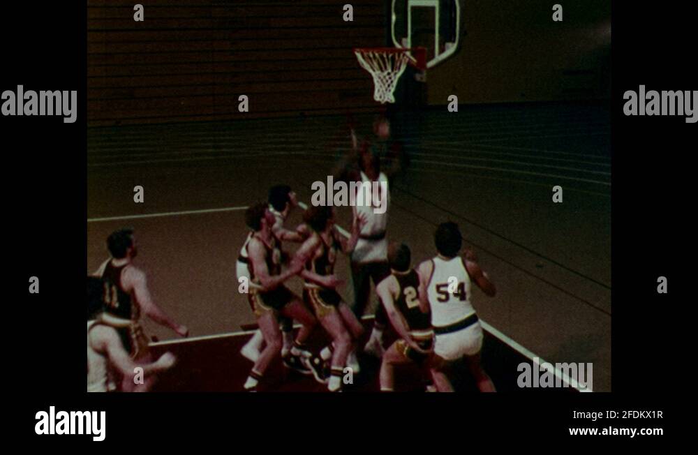 1970s: Referee shadows players on basketball court. Men play basketball ...