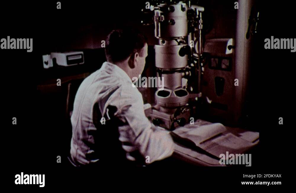 1960s: Man sits in front of electron microscope. Man looks into ...