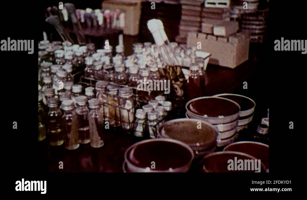 1960s: Vials, test tubes and petri dishes on counter. Two scientists at ...