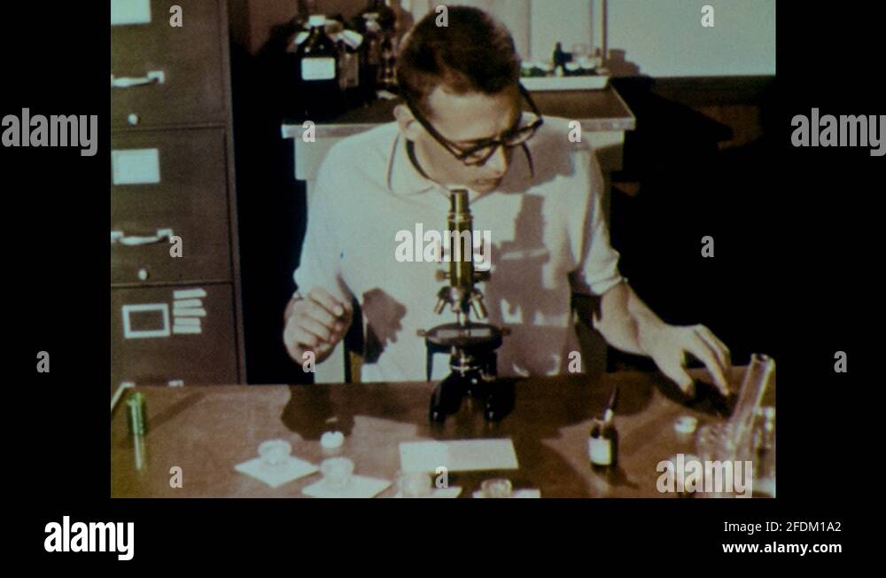 1960s: Lab, glass slide under microscope, man uses tweezers to place ...