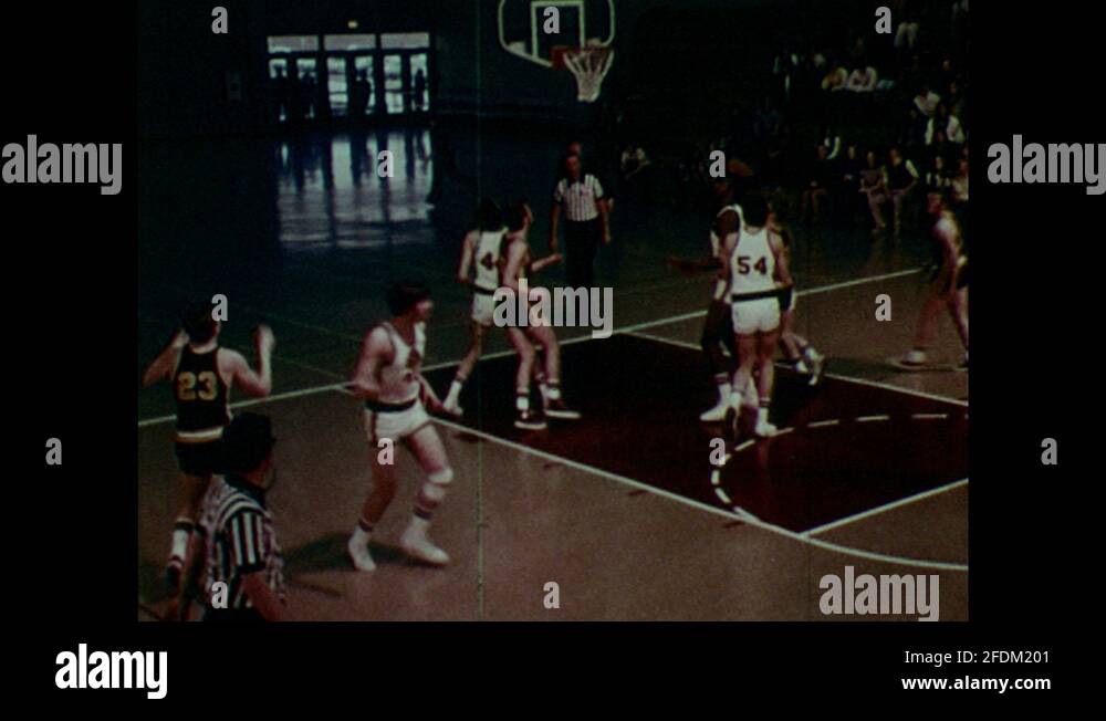 1970s: Men play basketball in gymnasium. Crowd and cheerleaders stand ...