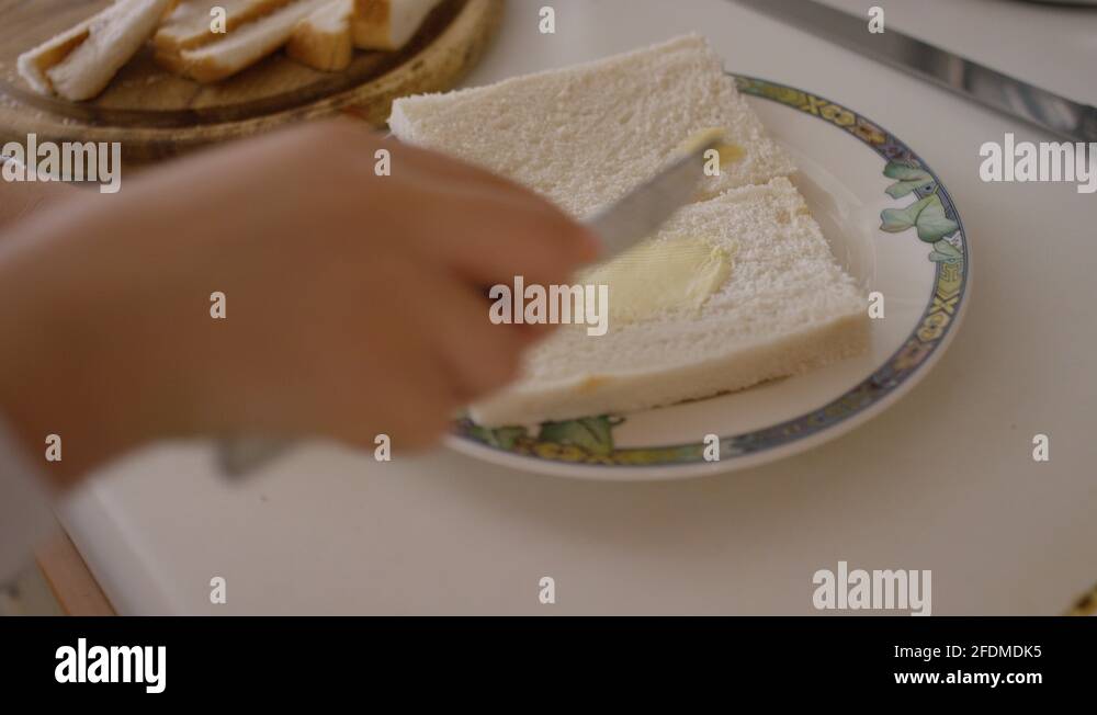 Young girl in the kitchen buttering bread as she prepares to make a ...