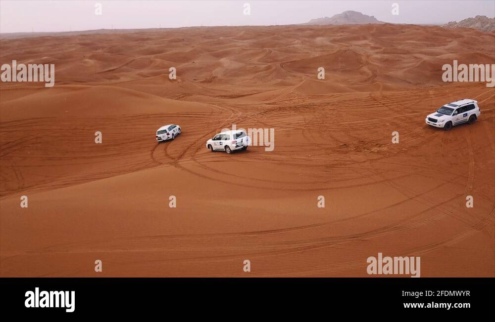 Following 4x4 vehicles in a red sand desert for desert safari. Drone ...