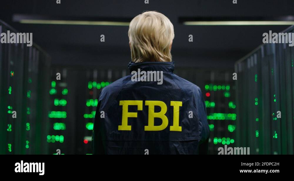 Rear of female FBI officer walking the dark corridor in server room ...