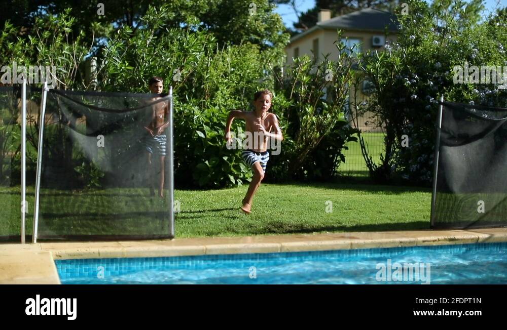 Two young boy running and jumping into swimming pool water in slow ...