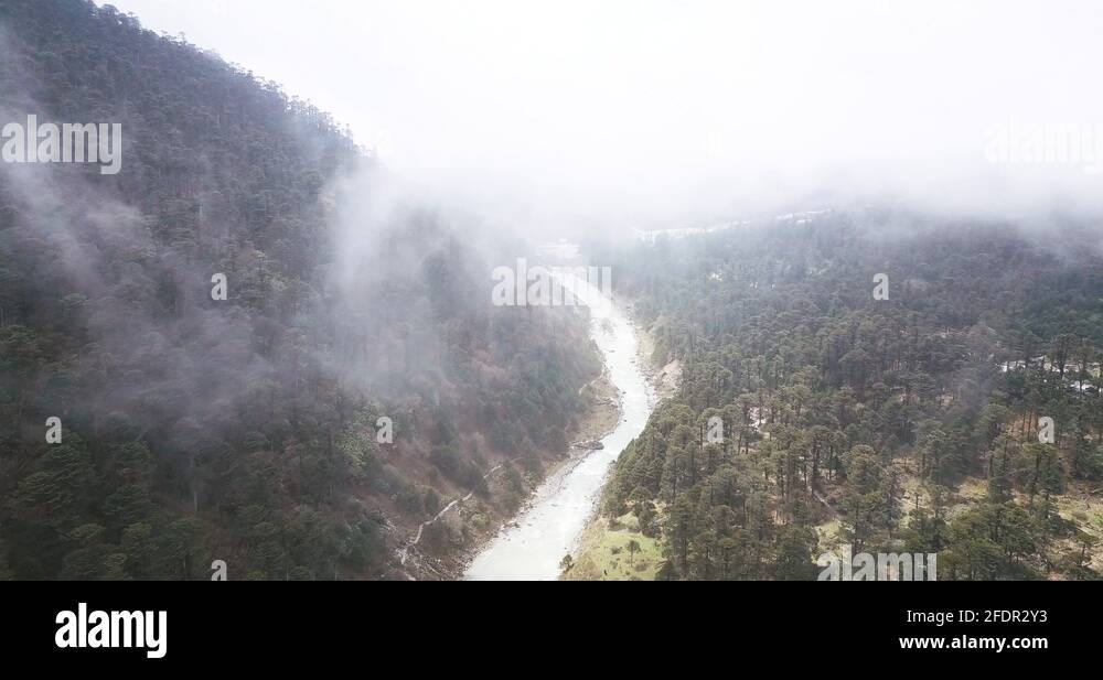Flying through clouds in misty valley with natural river and deep green ...