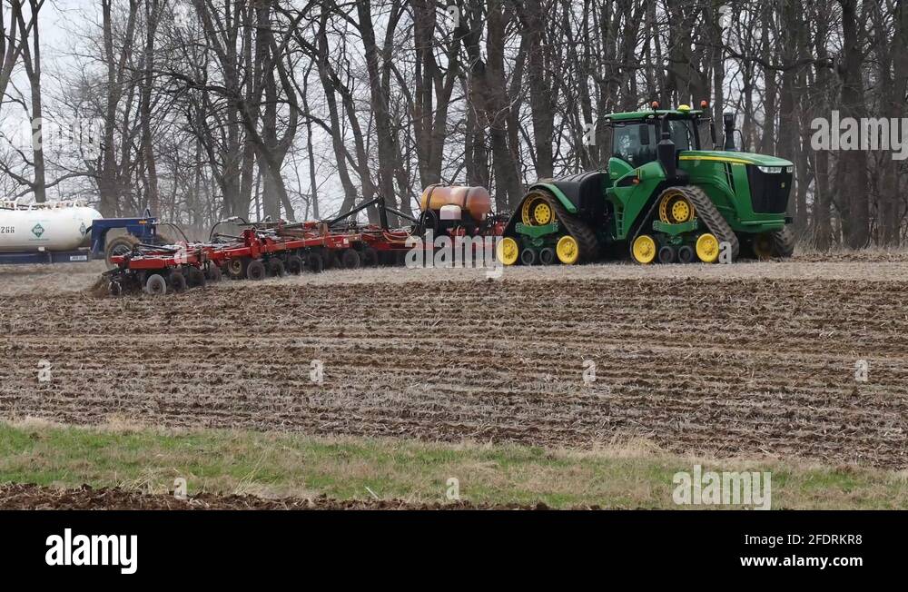 Belted John Deere tractor using planter and fertilizer tanks in field ...