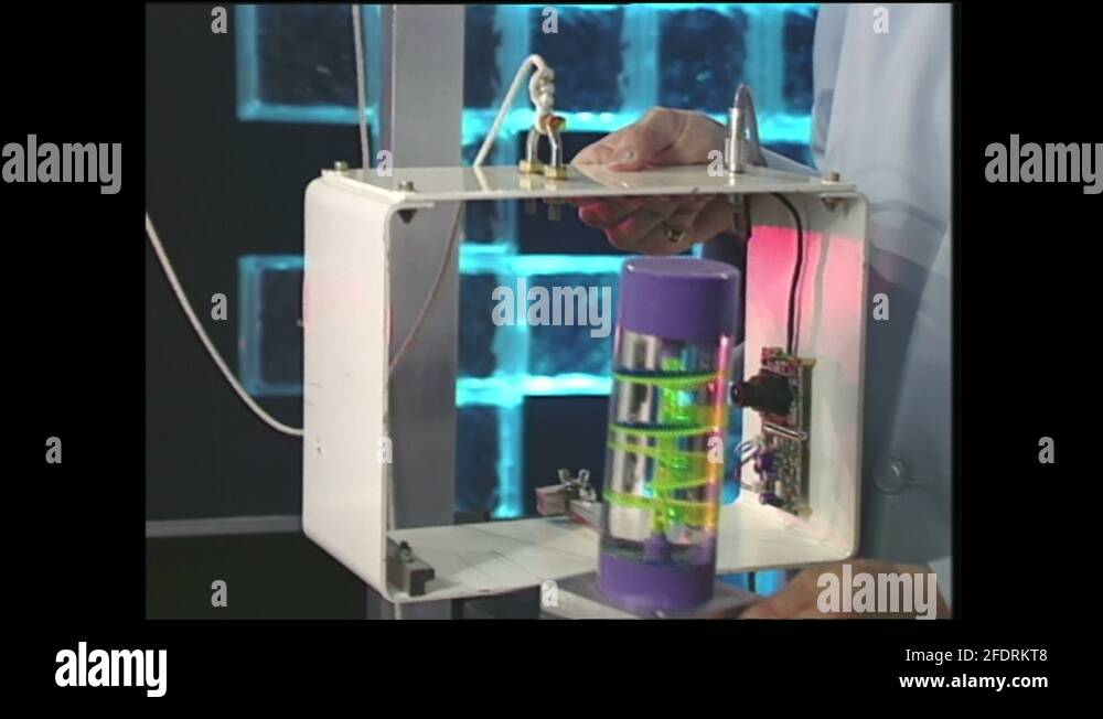 1990s: TV studio, woman mounts liquid cylinder toy on platform of drop ...