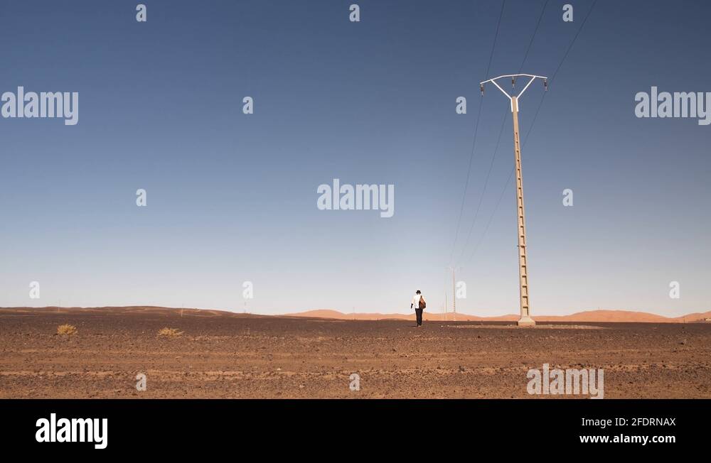 A lonely man walking into a black sahara desert electric pole on head ...