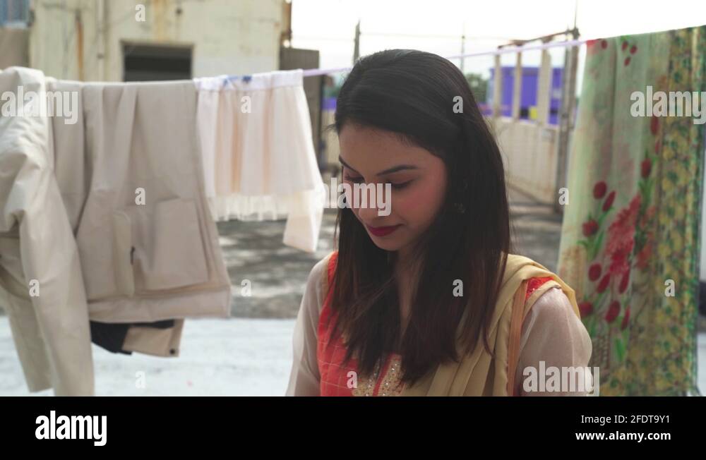 beautiful Indian girl hang clothes on clothesline and looks at someone ...