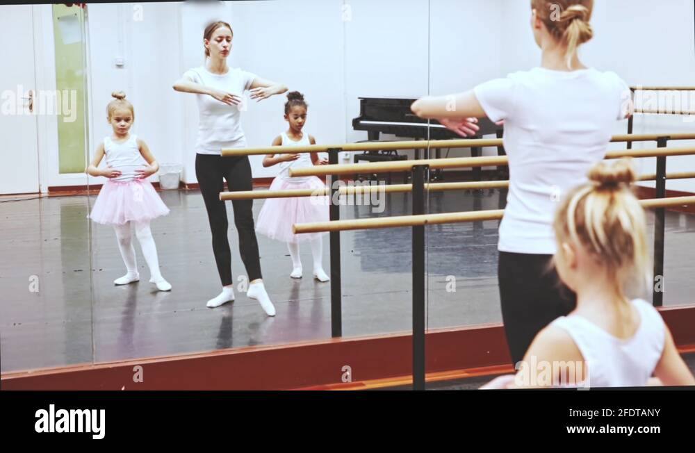 Young female classical dance teacher showing correct ballet position to ...