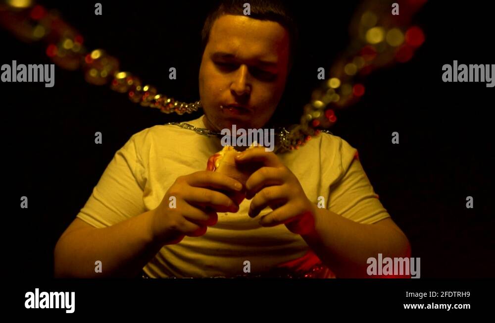 Fat man eating fast food whose chains are on his neck. Hostage concept ...