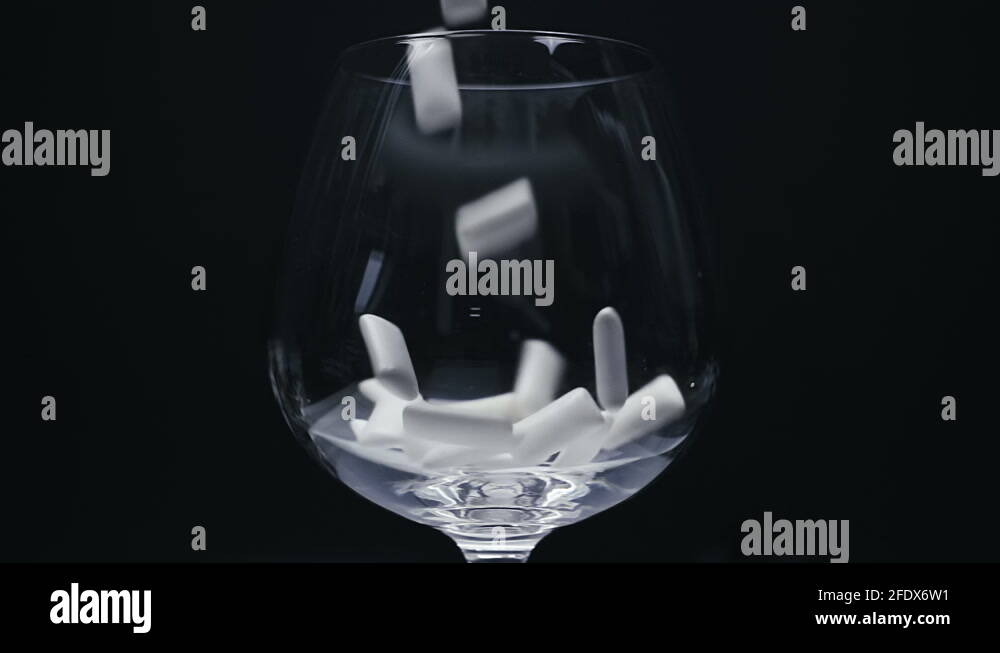 A heap of white chewing gum pads falling into a glass goblet on black ...