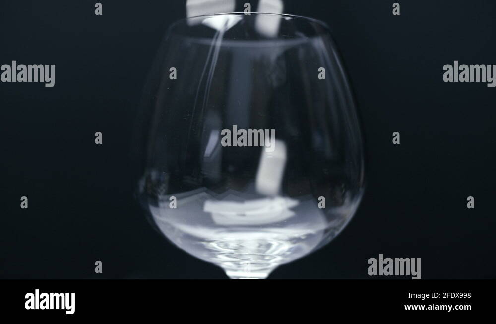 A heap of white chewing gum pads falling into a glass goblet on black ...