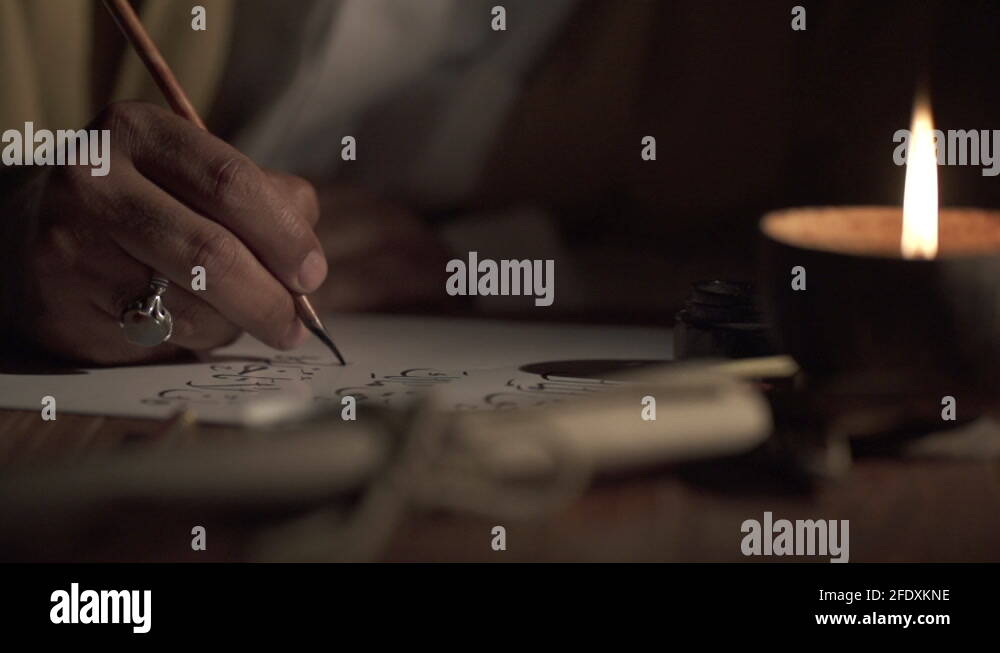 A medieval man uses an old pen with ink to write on an a paper lit by a ...