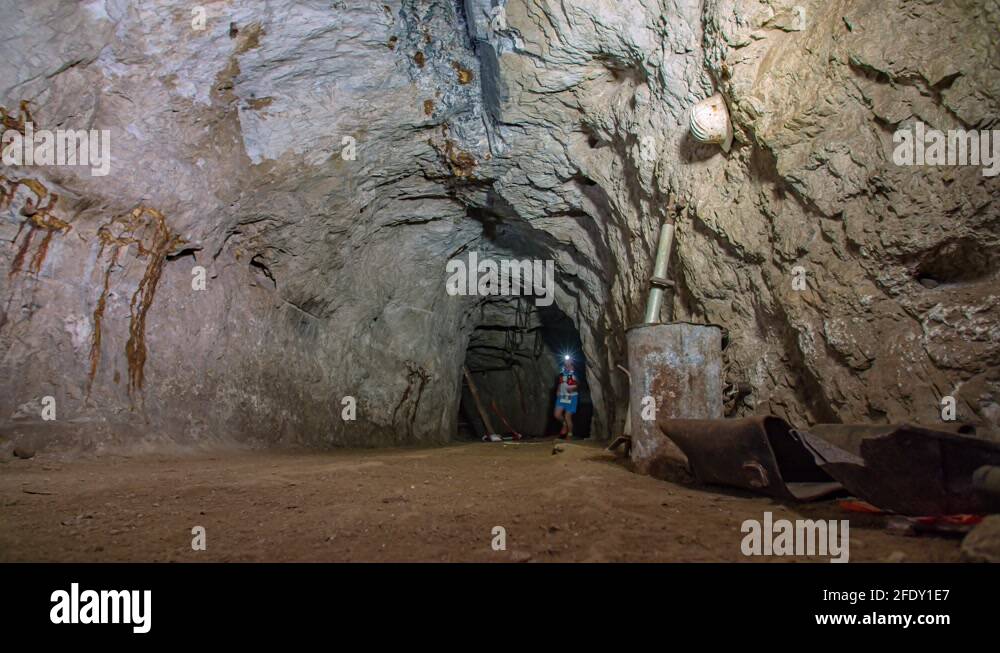 Two Caucasian men wearing headlights run in narrow stone cave tunnel in ...
