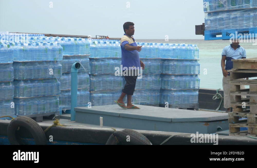 CLOSE UP: Dock workers load up a small cargo ship with pallets of ...