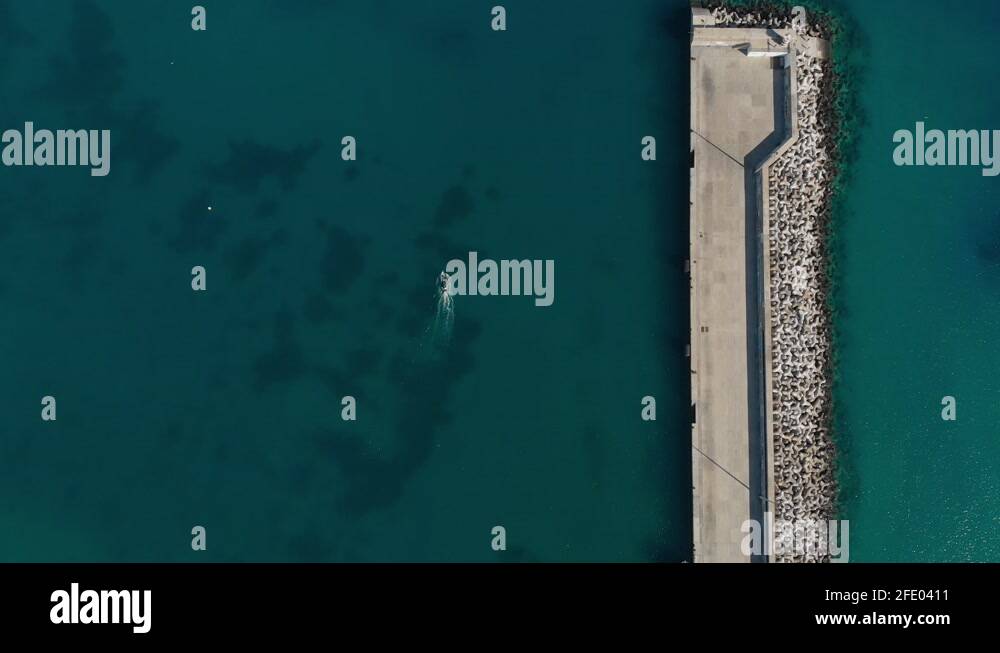 Top down shot Fishing boat leaving harbor with concrete pontoon blue ...