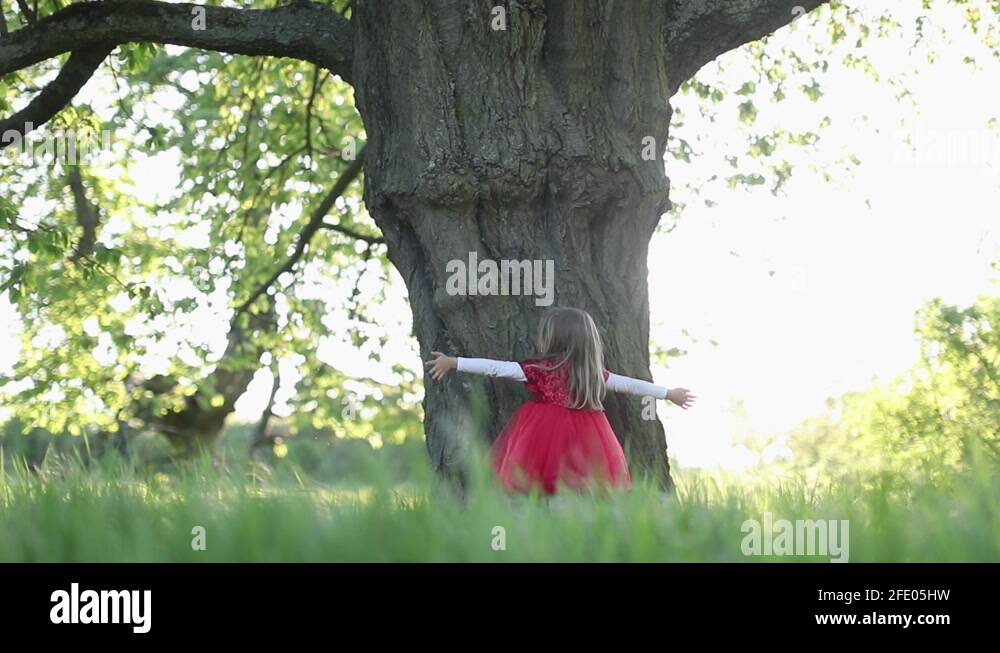 SLOW MOTION Happy cute blond little girl in red dress touch the tree ...