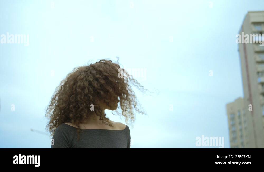 woman with curly hair turns her head on the street, the wind in her ...
