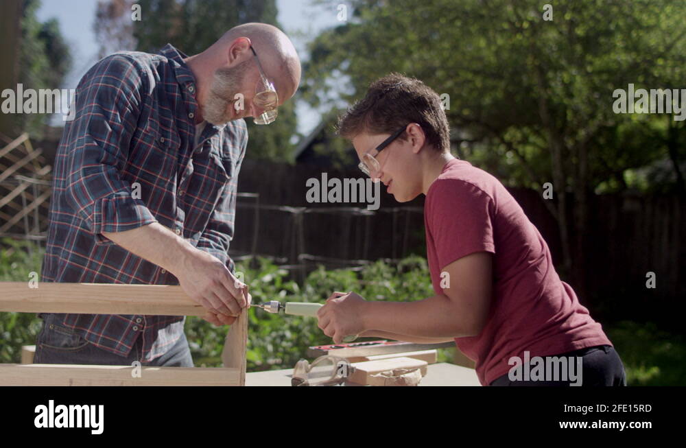 A father and son wearing safety glasses work on a DIY project with a ...