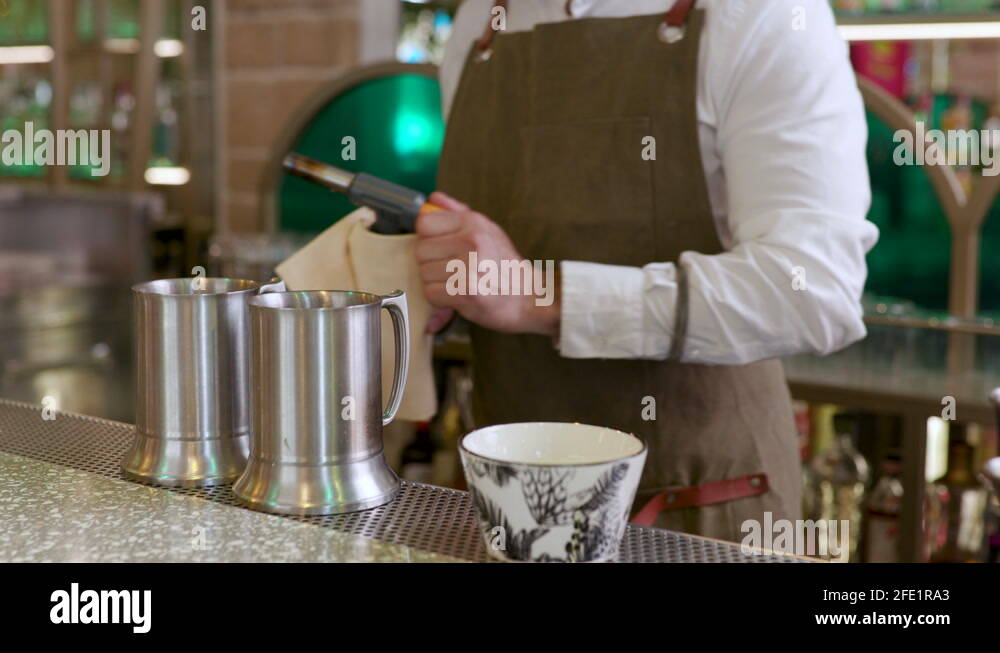 Two metal cups with high alcoholic liquid inside. The Barman lights the ...