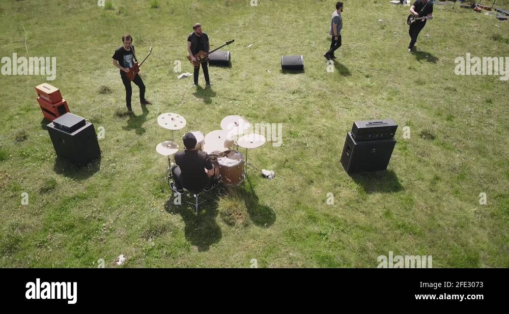 Five men from a rock band are playing outdoor in a forest clearing ...