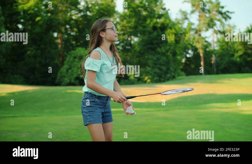 Girl playing badminton in field. Teen hitting shuttlecock with ...