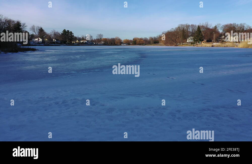 Low ice height drone high speed pass on frozen lake with white houses ...
