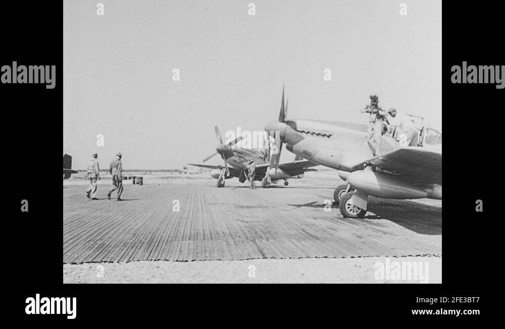 1940s: Soldiers and pilots walk around planes on runway. Pilots squat ...