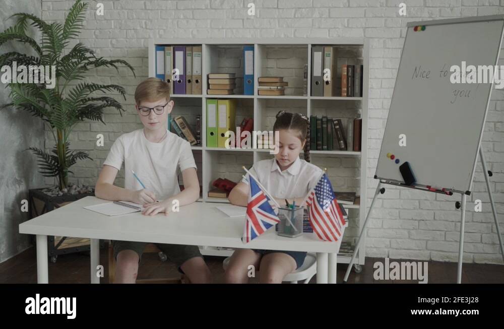 Young learners boy and girl in a classroom writing with pencil writing ...