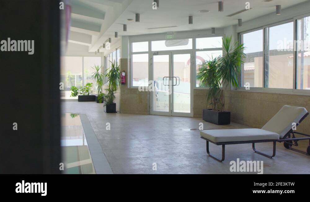 Massive indoors pool with a shezlong chair and a glass wall, inside a ...