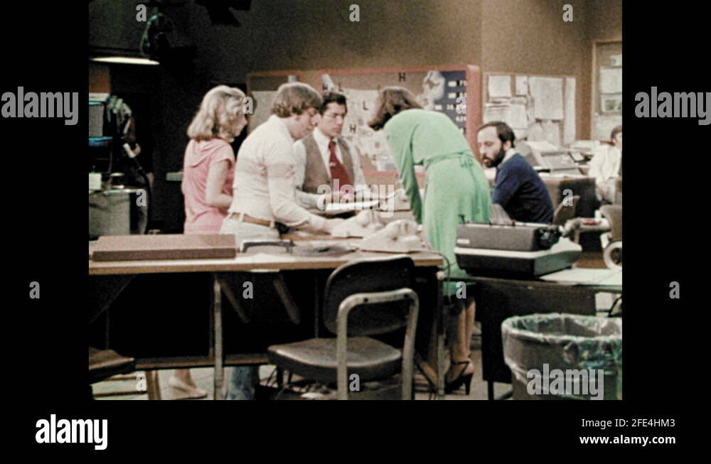 Television station, people huddle over desk, look at papers. Jay ...