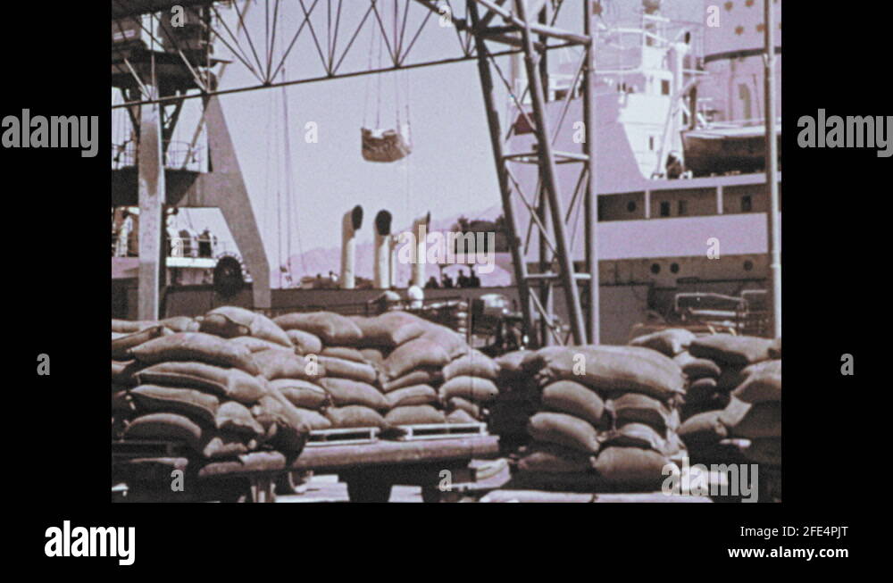 1970s: Cargo is unloaded by crane from boat at dock. Cruise ship and ...