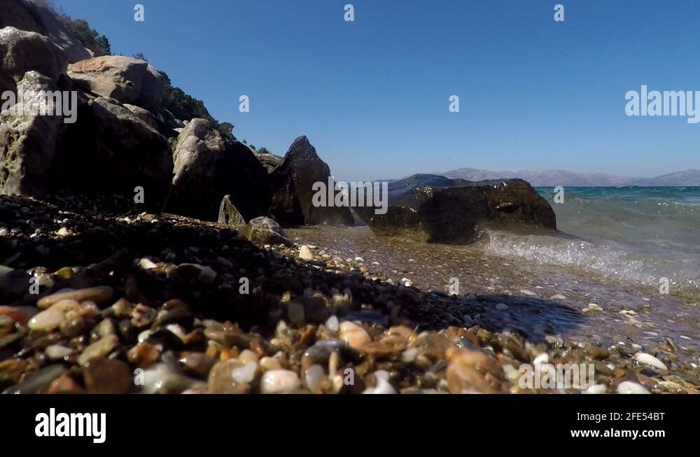 Ground level footage of sea waves splashing on a beach of pebbles, at ...