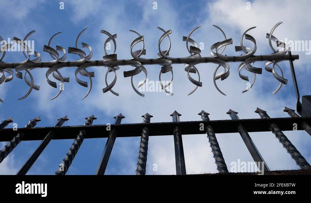 Prison barbed wire steel gate looking up to blue cloudy sky dolly left ...