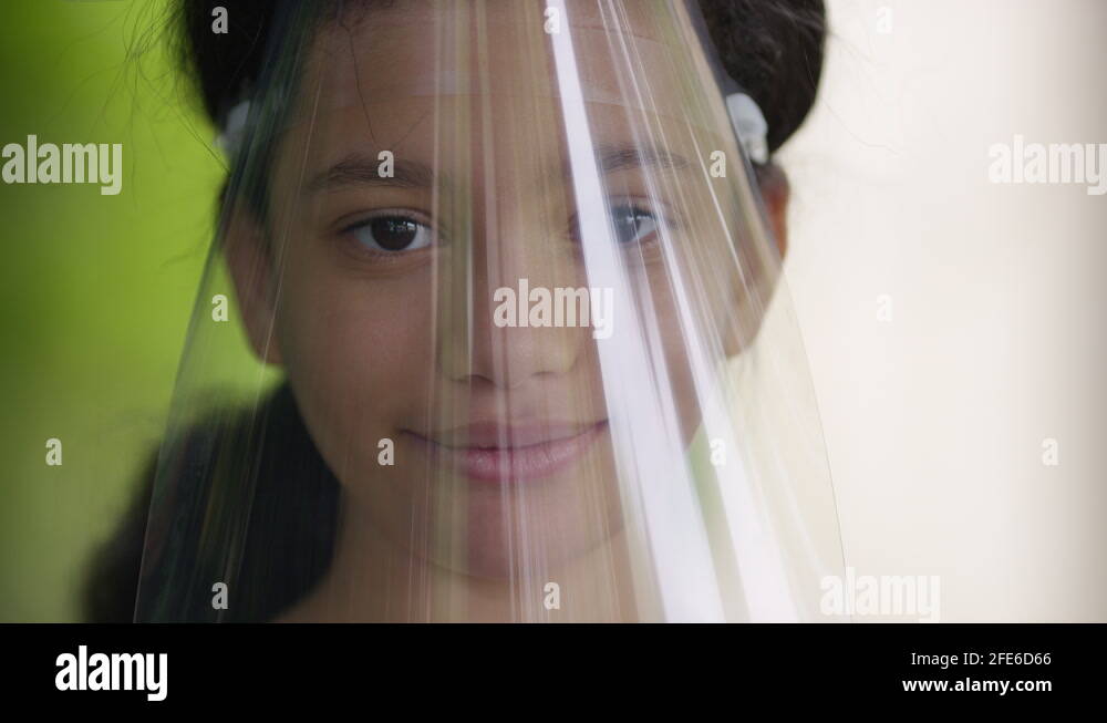 Portrait of little girl with a subtle smile wearing a face shield for ...