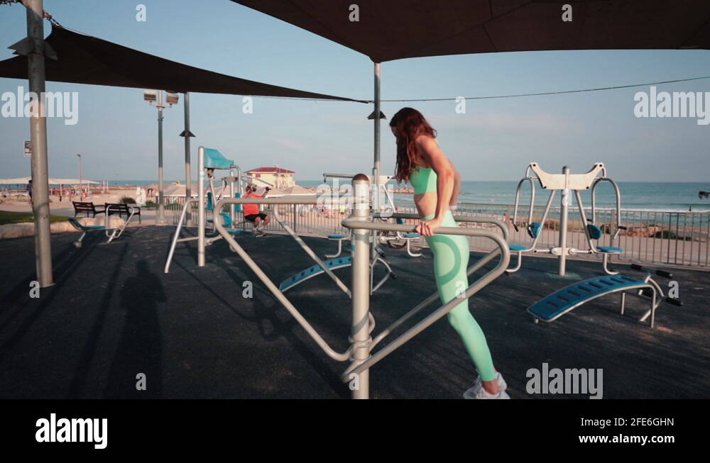 Muscular slim woman lifting herself on parallel bars in an outdoor gym ...