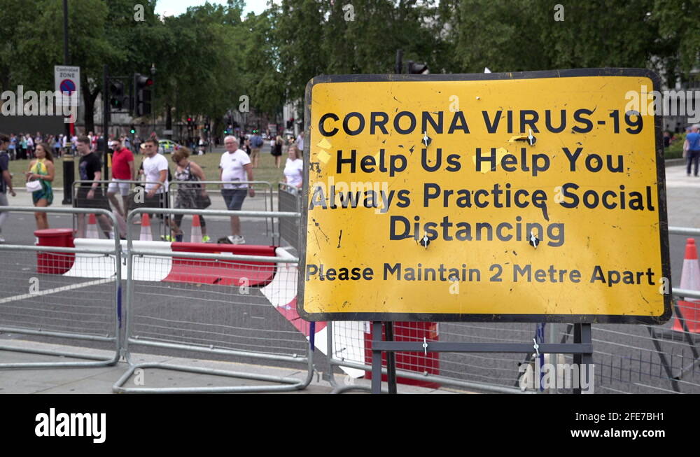 People cross a pedestrian crossing behind a yellow information road ...