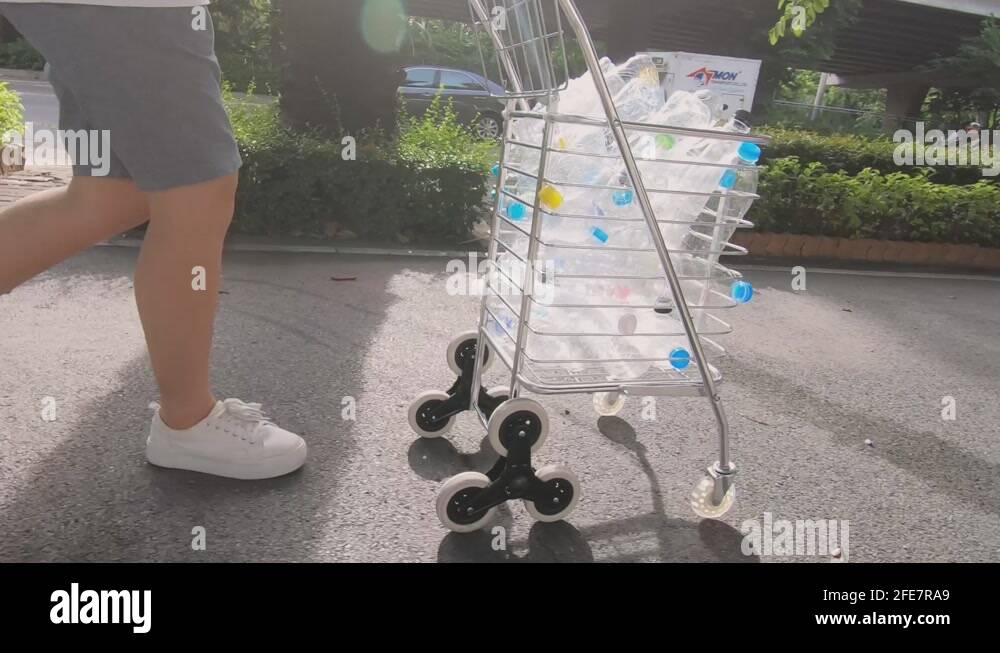a man walking and pulling cart full of plastic bottles goinf to recycle ...